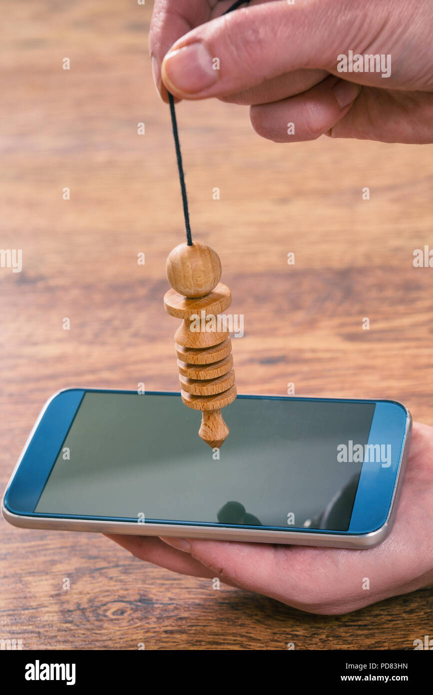 Hand with pendulum dowsing over smart phone to check its quality ...