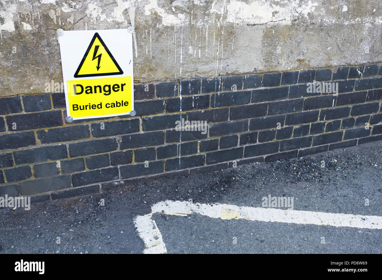Buried electrical cable danger sign with arrow on ground road pavement ...
