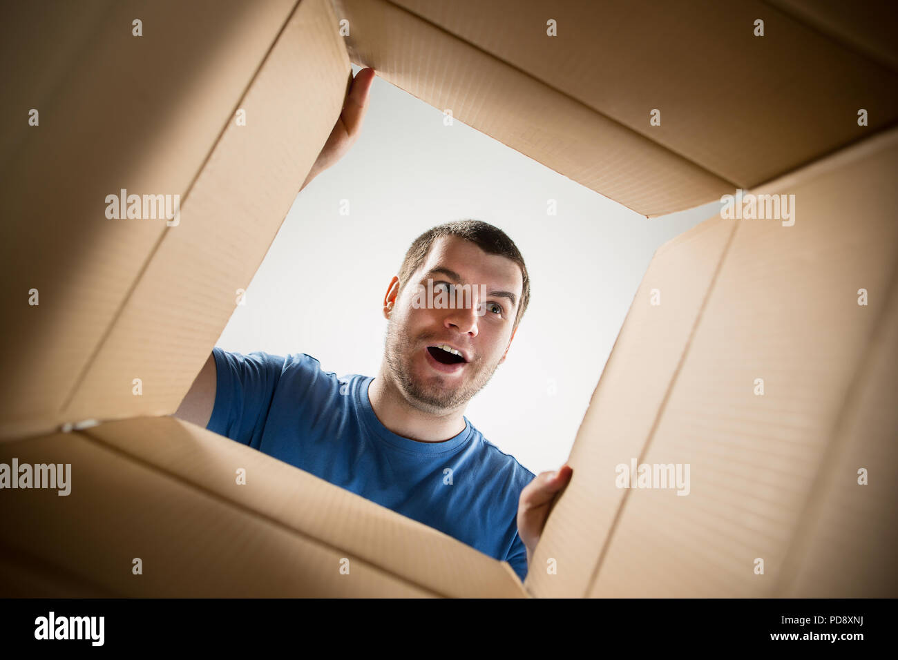 The surprised man unpacking, opening carton box and looking inside. The ...