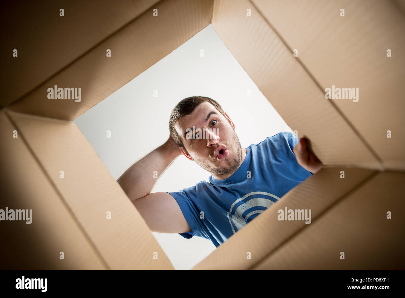 The surprised man unpacking, opening carton box and looking inside. The ...