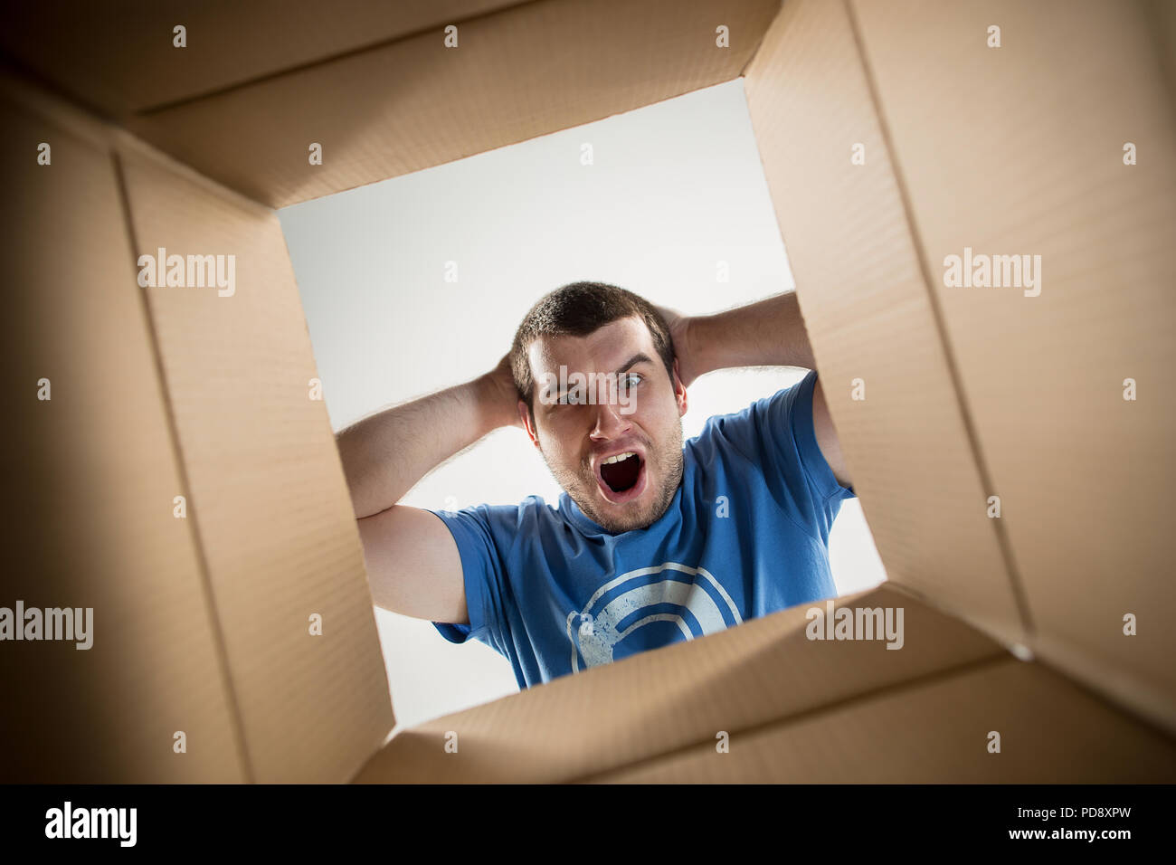 The surprised man unpacking, opening carton box and looking inside. The ...