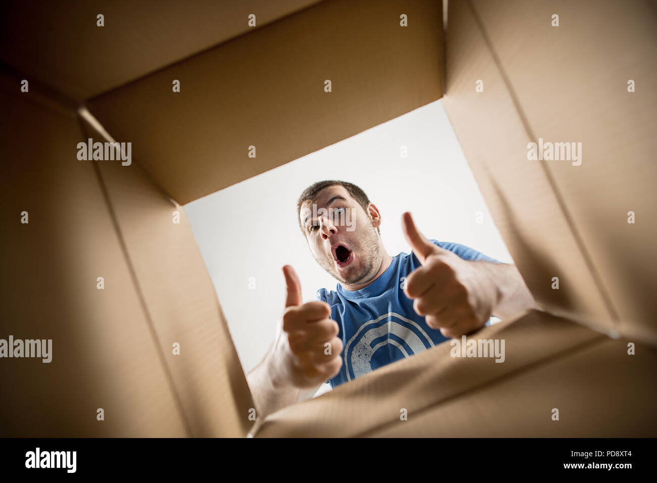 The surprised man unpacking, opening carton box and looking inside. The ...