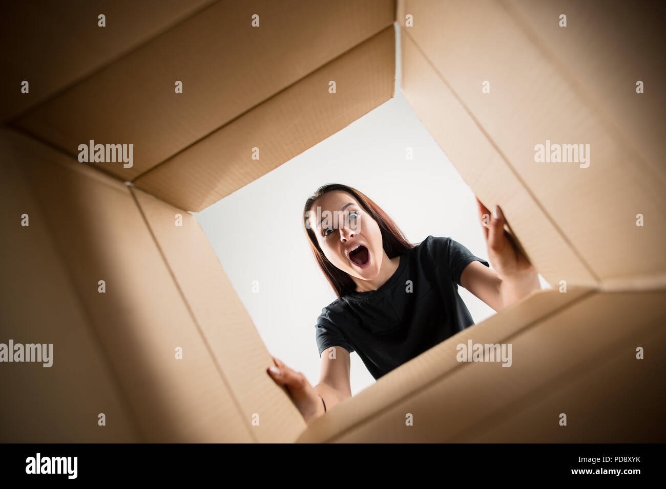 The surprised woman unpacking, opening carton box and looking inside ...