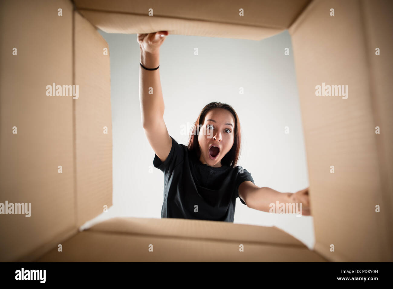 The surprised woman unpacking, opening carton box and looking inside ...