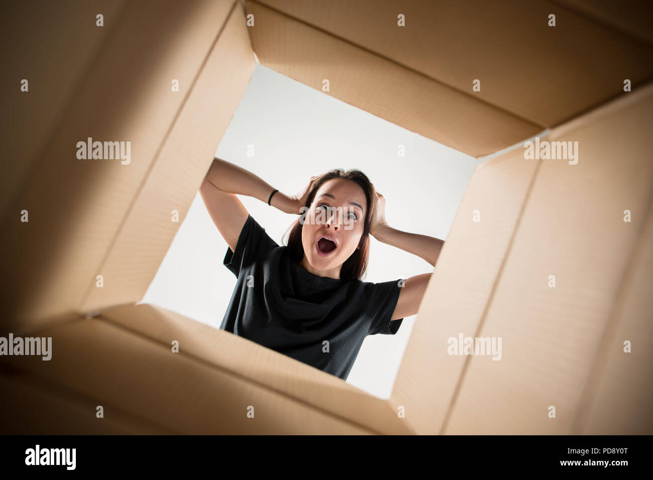 The surprised woman unpacking, opening carton box and looking inside ...