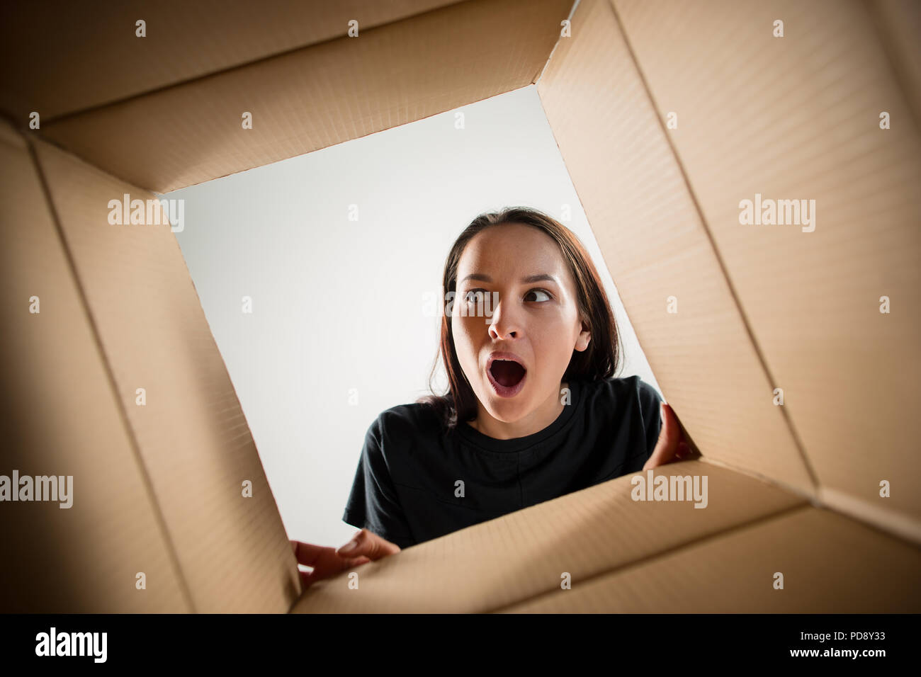 The surprised woman unpacking, opening carton box and looking inside ...