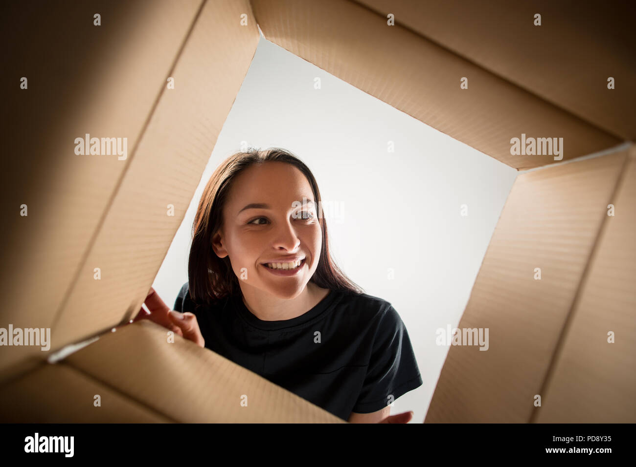 The surprised woman unpacking, opening carton box and looking inside ...
