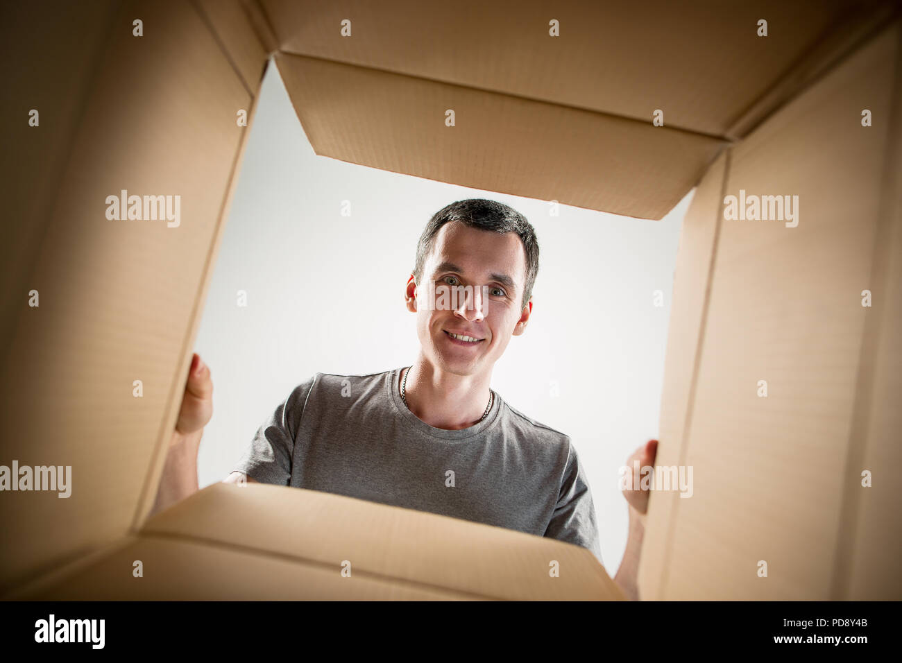 The surprised man unpacking, opening carton box and looking inside. The ...