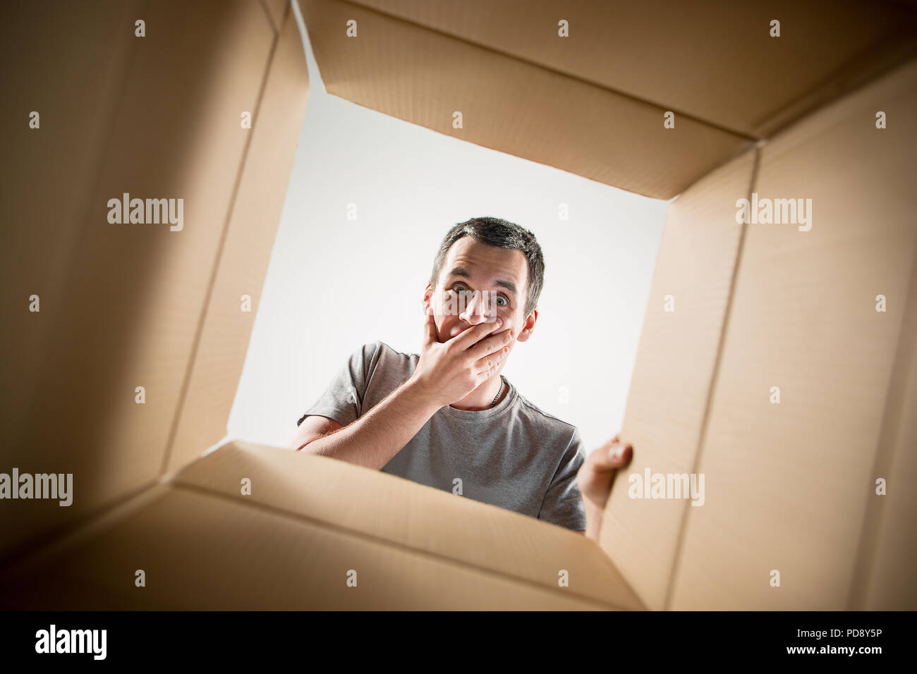 The surprised man unpacking, opening carton box and looking inside. The ...
