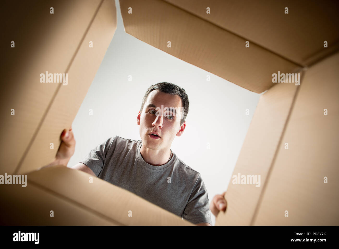 The surprised man unpacking, opening carton box and looking inside. The ...