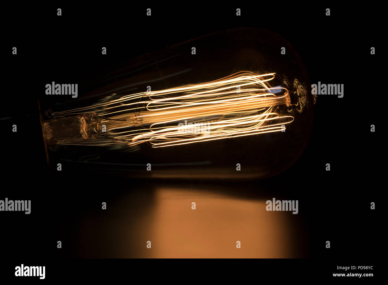 Light Bulb showing glowing filament. Reflective light on a shiny black ...