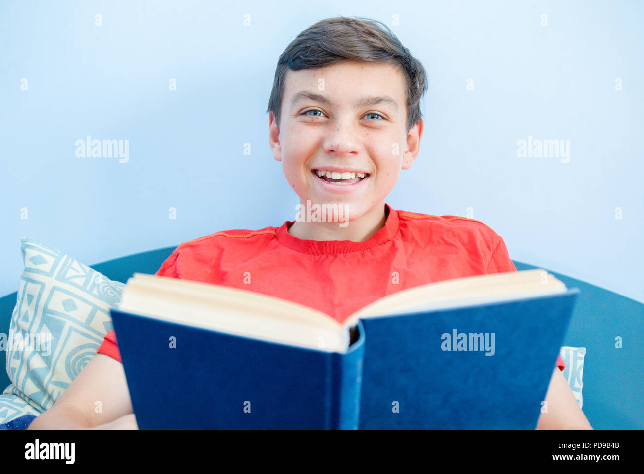 Caucasian teenage boy reading a book laying on a bed laughing Stock ...