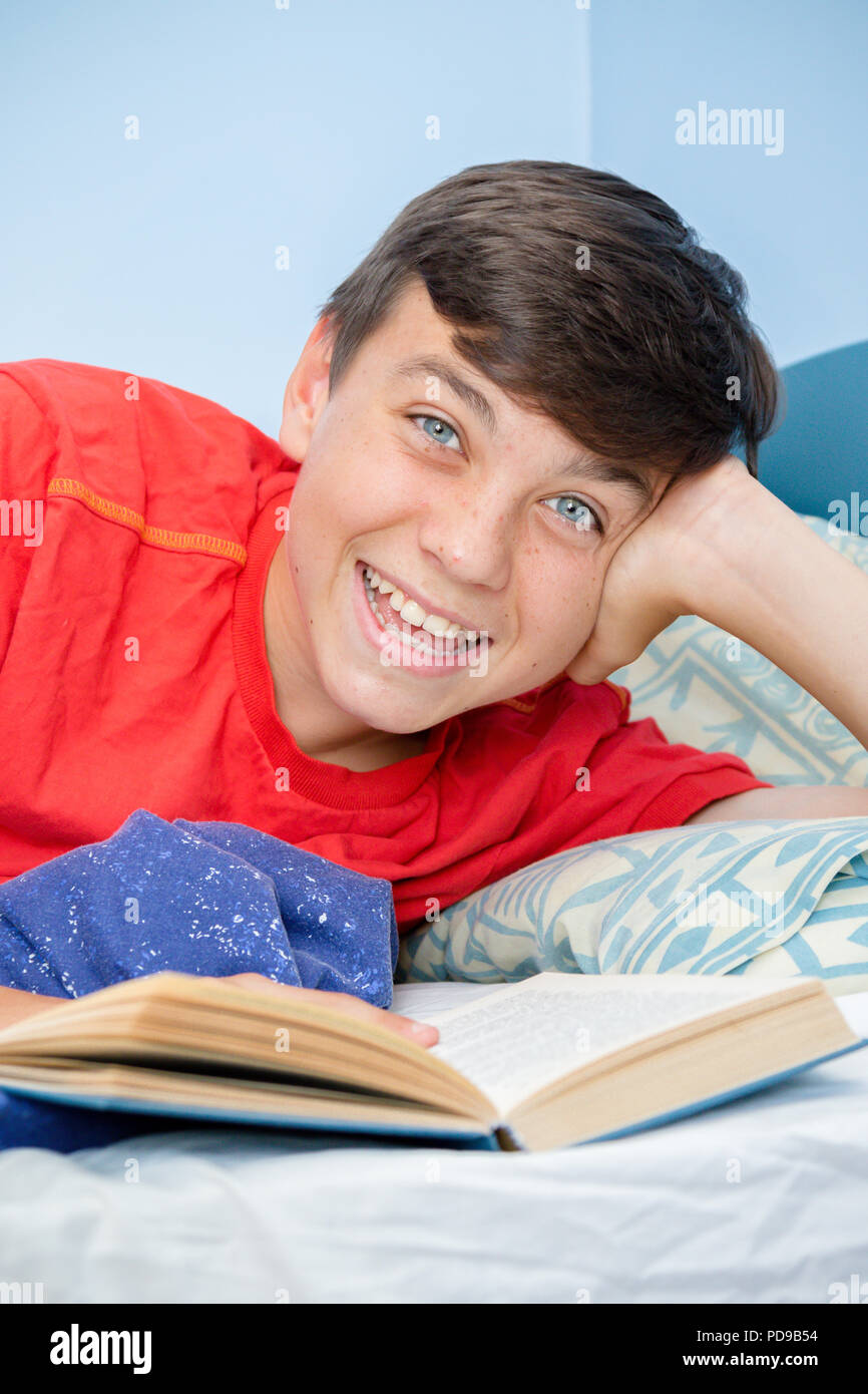 Caucasian teenage boy reading a book laying on a bed laughing Stock ...