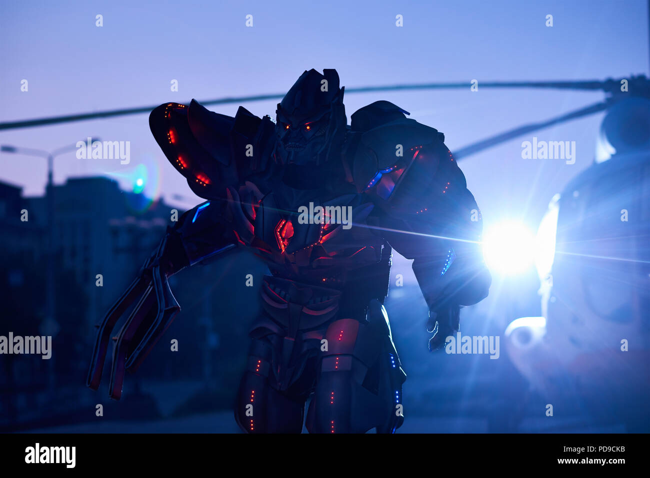 Impressive robot-transformer standing near military helicopter. Dark ...