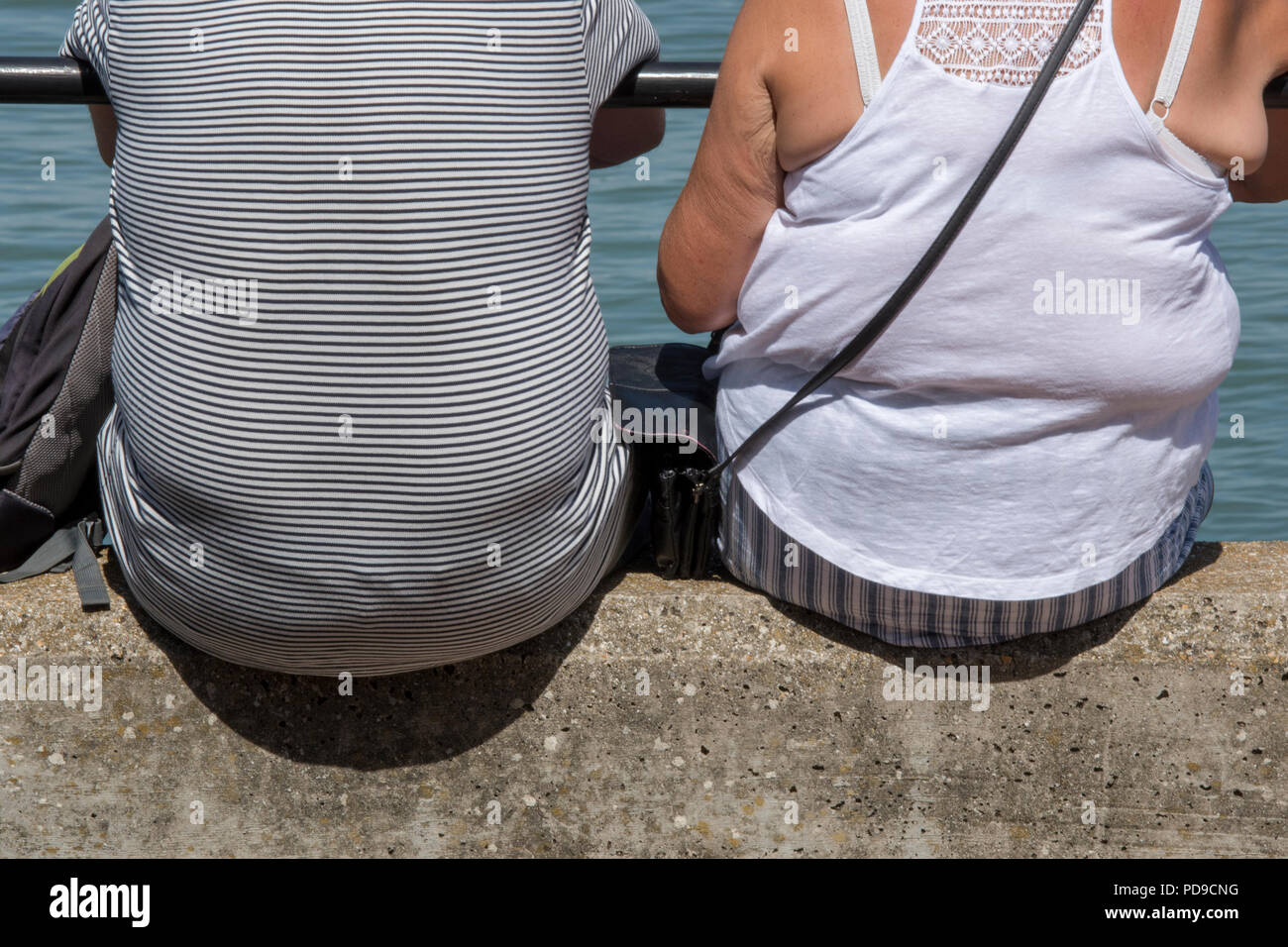 belly fat on two middle aged people sitting on a wall. Obesity and ...