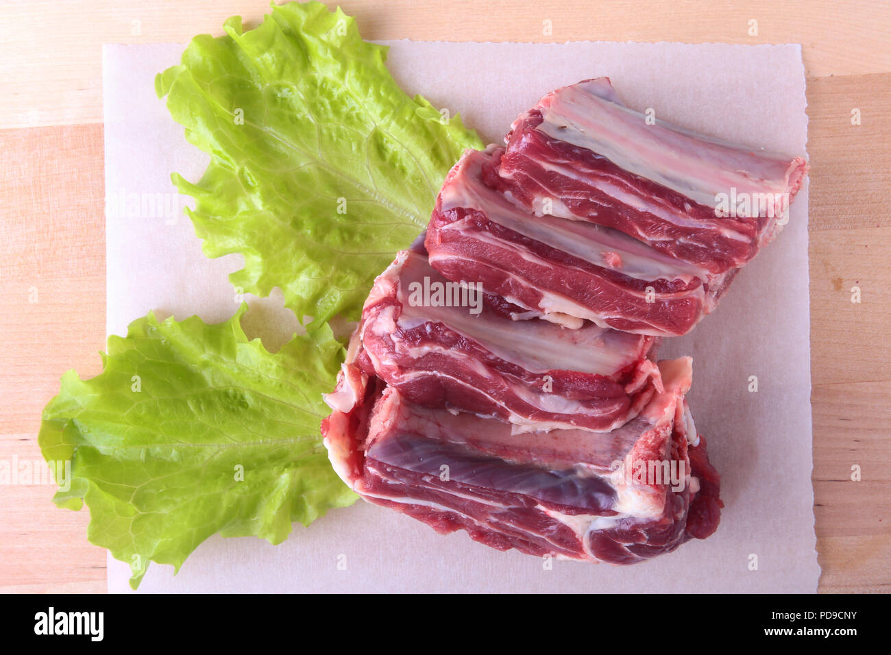 Raw beef edges and lettuce leaf on wooden desk isolated on white ...