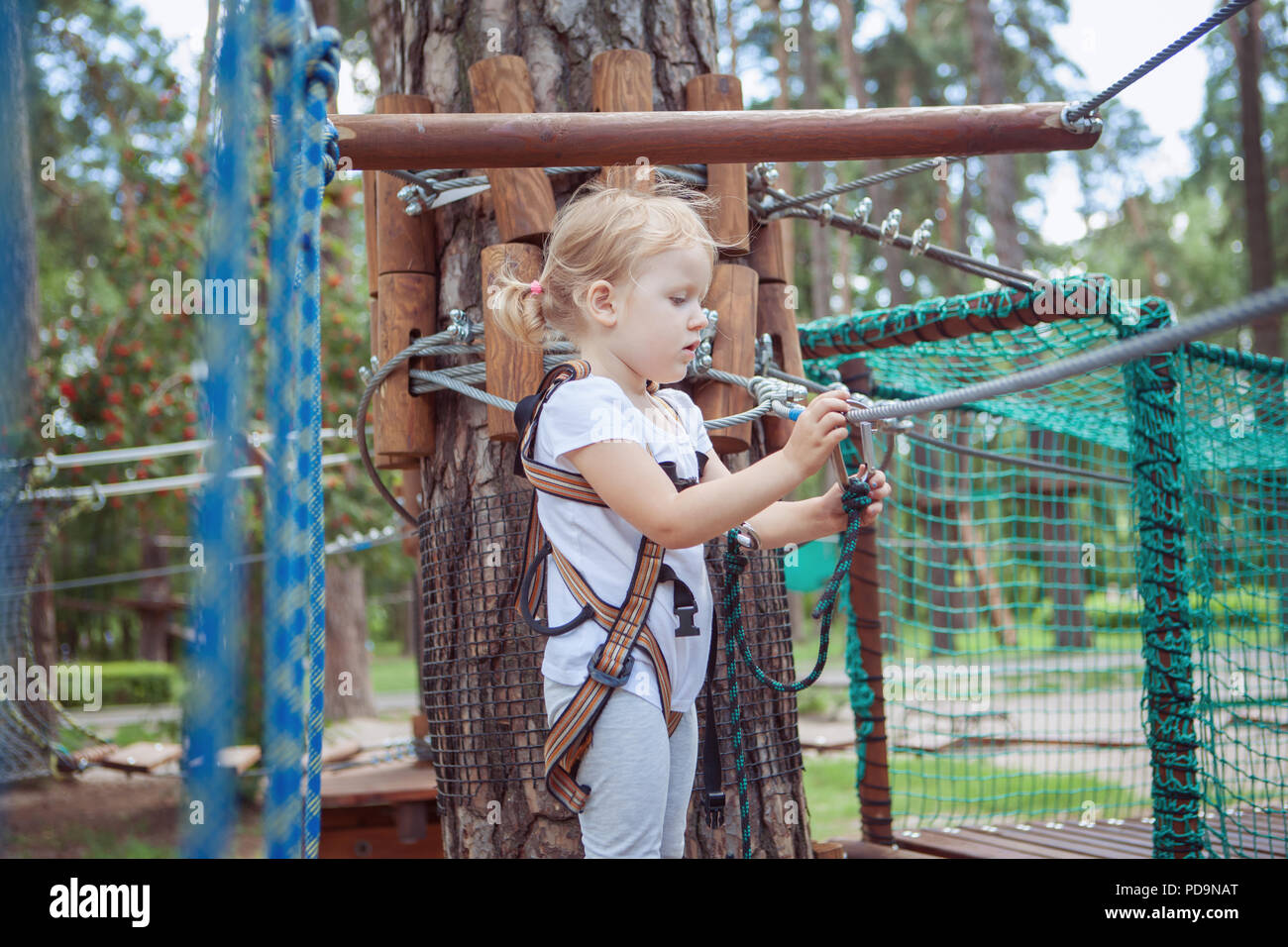 Portrait of a little blond girl in rope park. She attaches carbines ...
