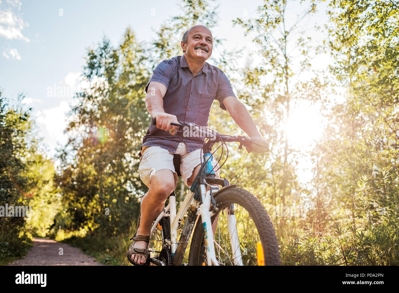Joyful senior man riding a bike in a park on a beautiful sunny day ...