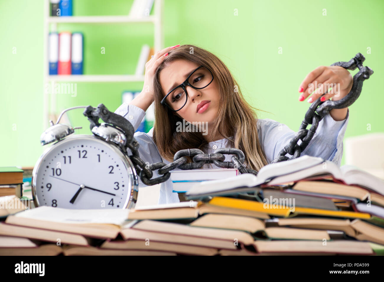 Young female student preparing for exams with many books and chained to ...