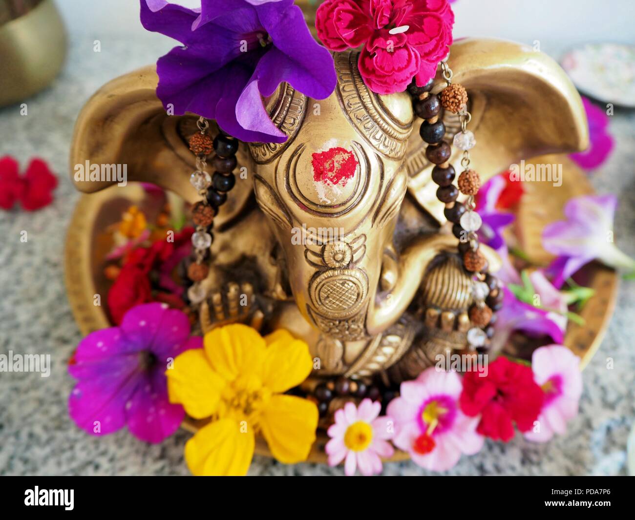 Hindu God Ganesha is covered with coloured flowers on an altar for a ...