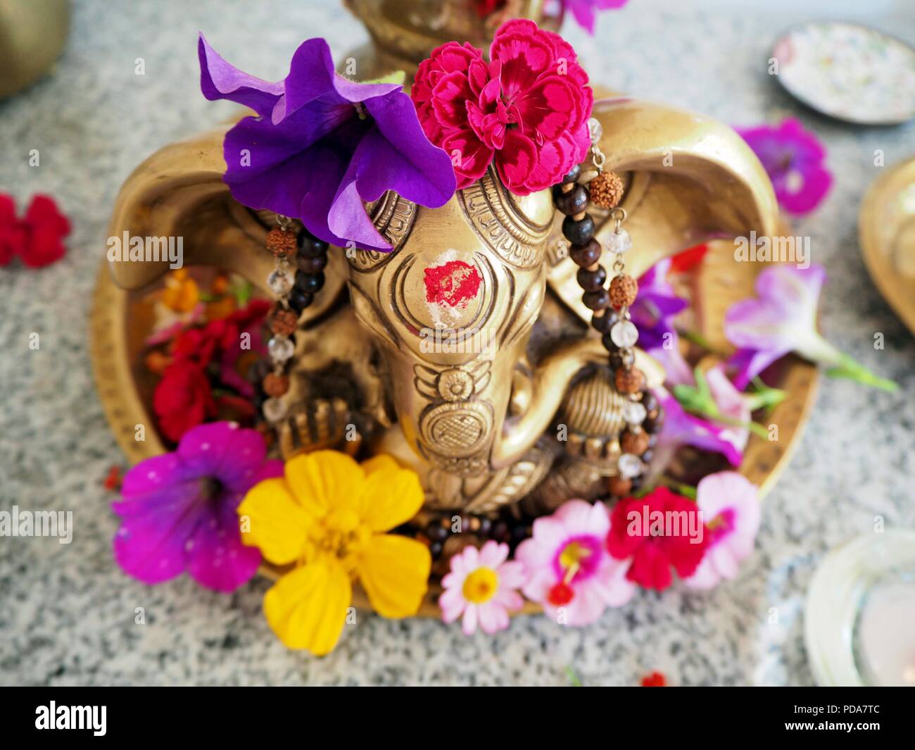 Hindu God Ganesha is covered with coloured flowers on an altar for a ...