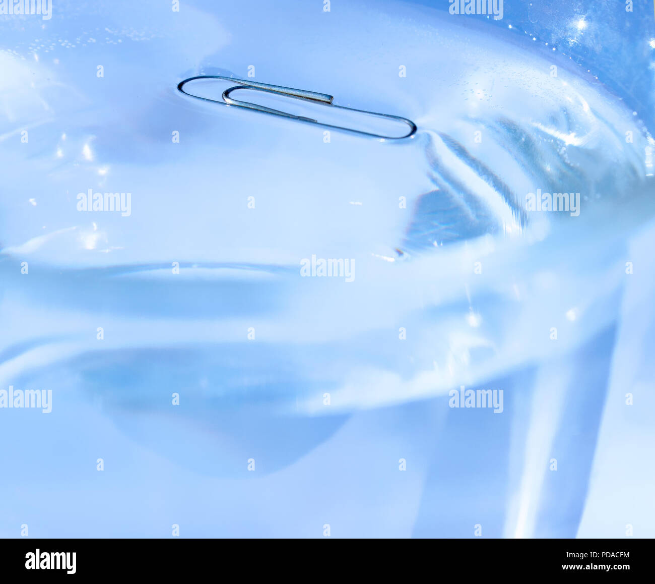 The isolated paper clip in a glass of water floats on the water surface ...
