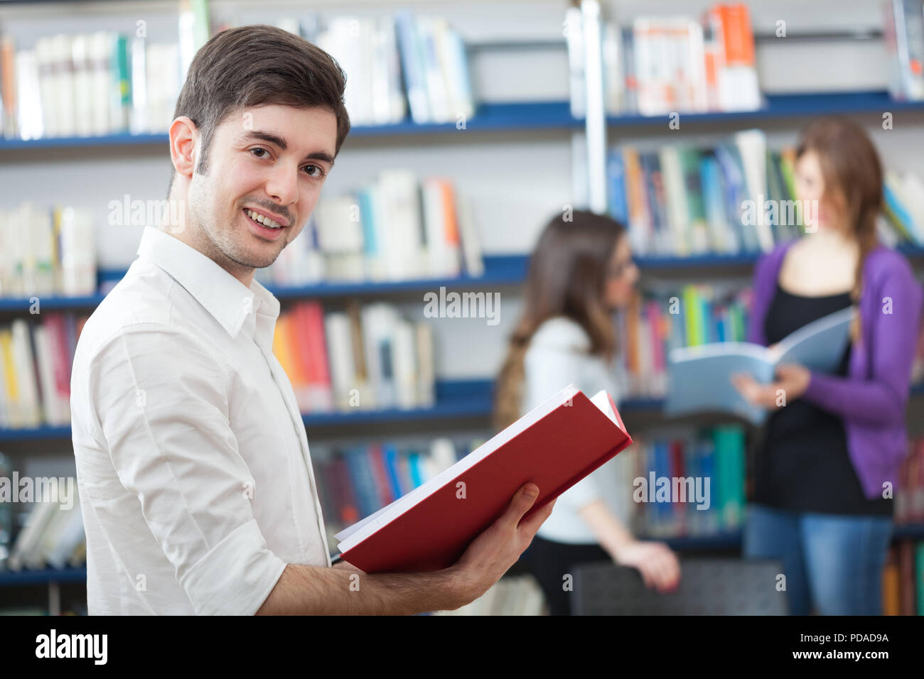 Young man reading a book in a library Stock Photo - Alamy