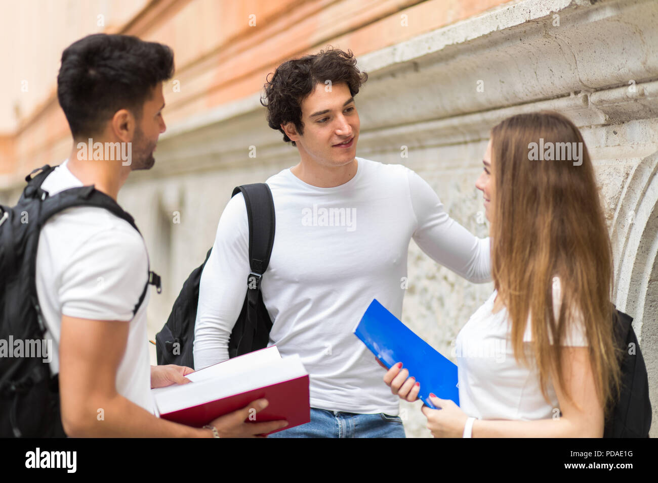 Three students talking to each other outdoor in a college courtyard ...