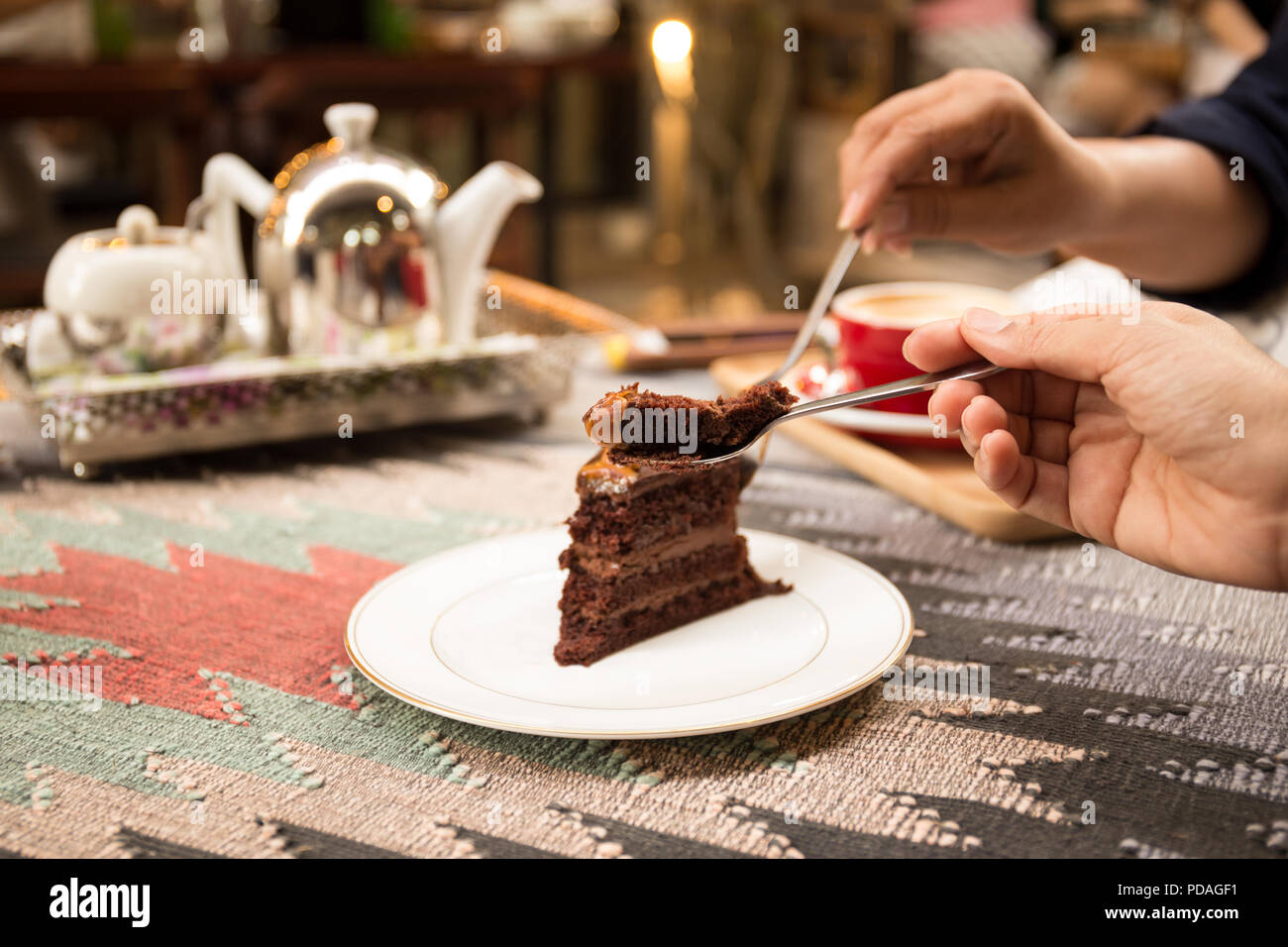 Woman's hand cutting slice of chocolate cake with tea pot in background ...