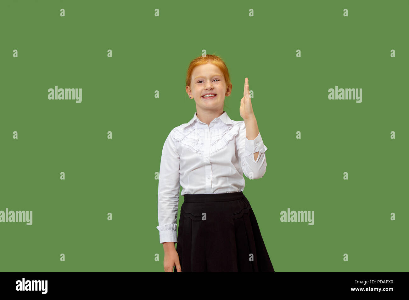 Happy teen girl standing with hand up, smiling isolated on trendy green ...