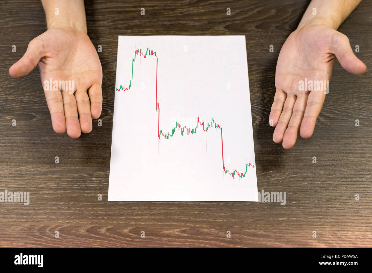 Man sitting at table. There are sheet of paper with a trading chart on ...