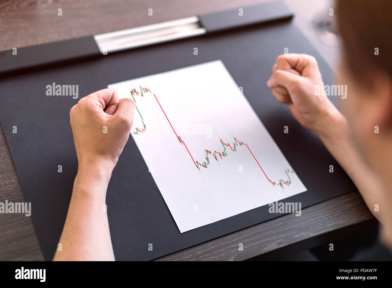 Man sitting at table. There are sheet of paper with a trading chart on ...