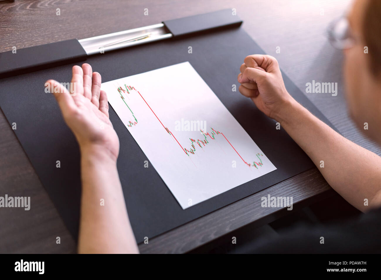Man sitting at table. There are sheet of paper with a trading chart on ...
