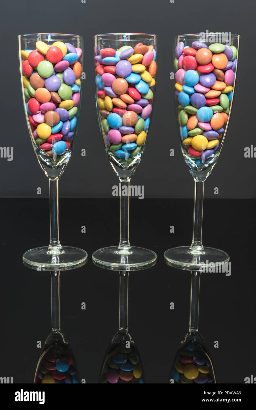Three champage flute glasses filled with smarties and isolated on black ...