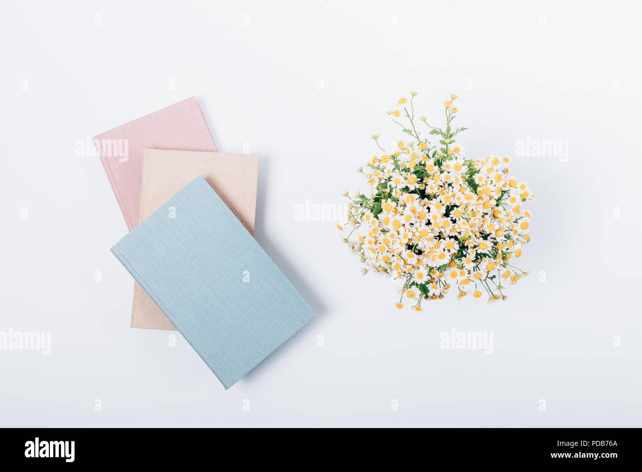 Feminine desk with a bouquet of small daisies and stack of three books ...