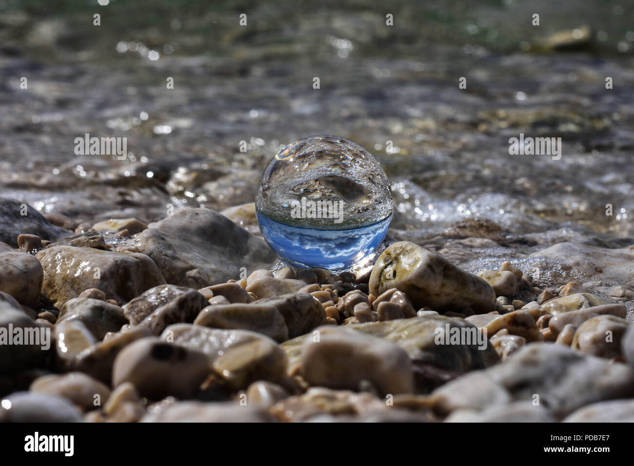 Glass ball sitting at rocky beach whit sea wave reflected in it ...