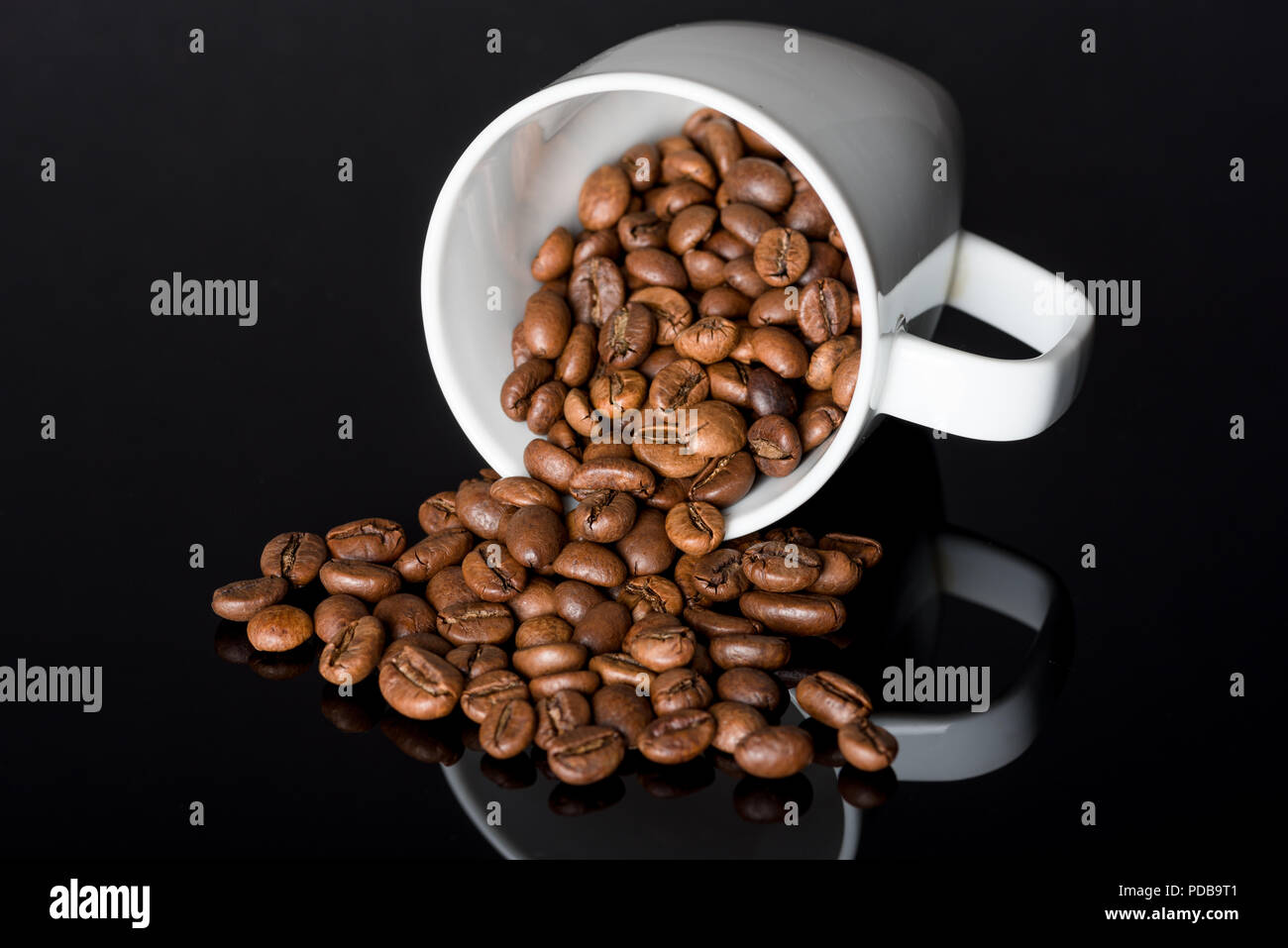 Roasted coffee beans spilling from white espresso cup lying on side on ...