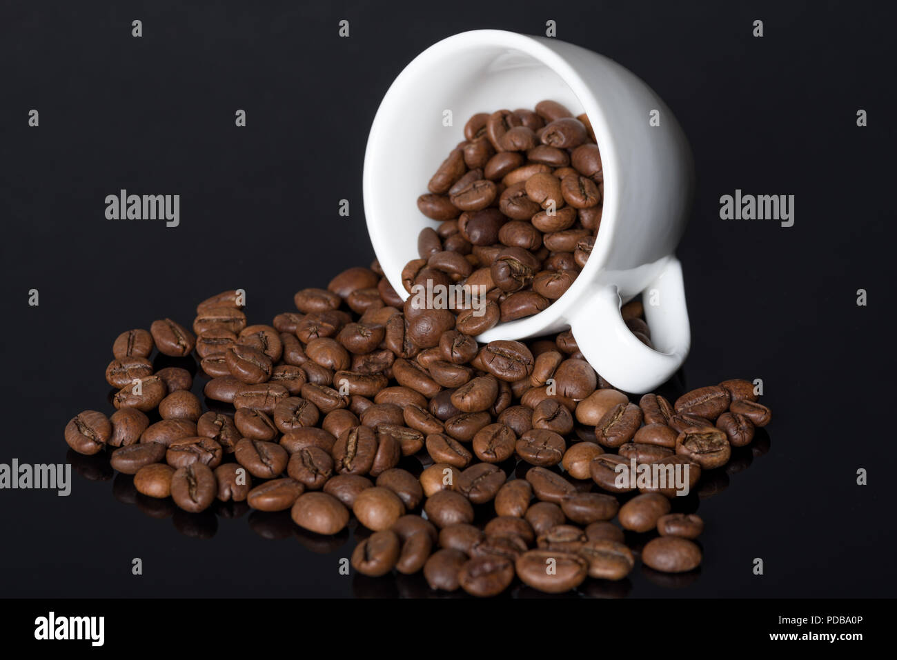 Roasted coffee beans spilling from white espresso cup lying on side on ...