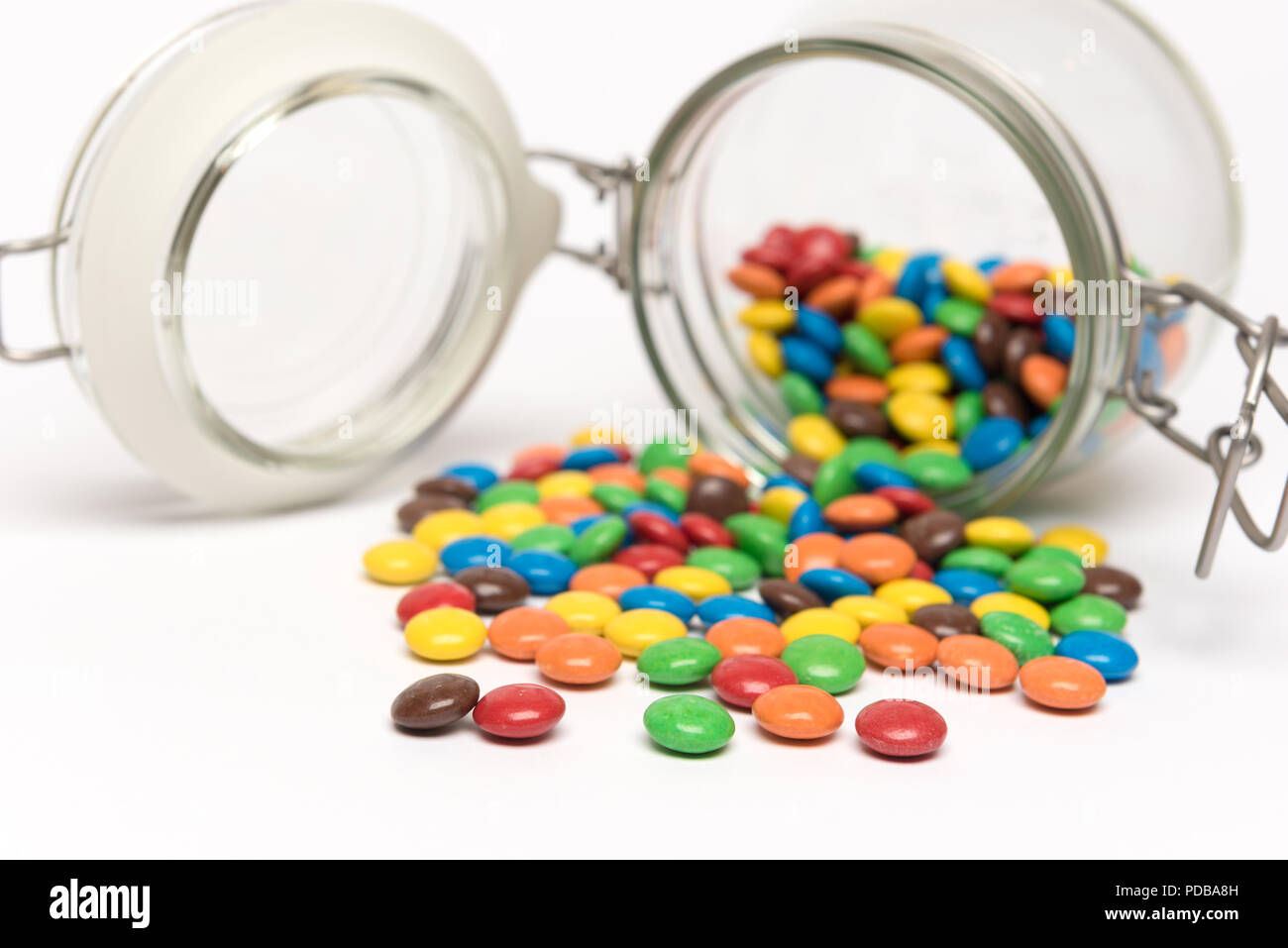 Colorful M&Ms spilling from a glass food storage jar lying on its side ...