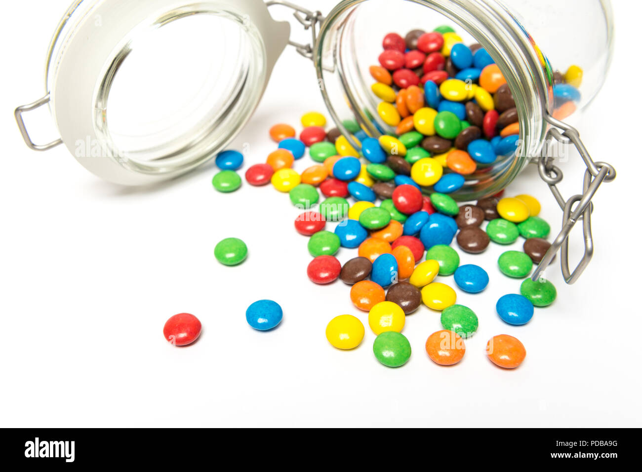 Colorful smarties spilling from a glass food storage jar lying on its ...