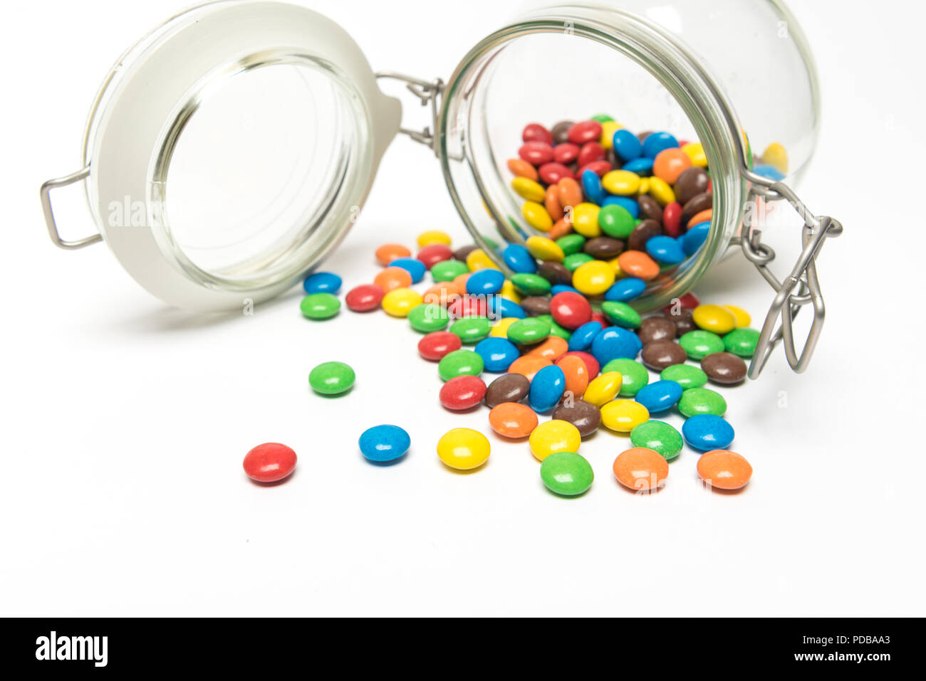 Colorful smarties spilling from a glass food storage jar lying on its ...