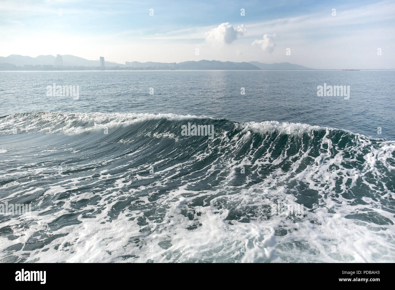 Deep green ocean wave with mountain and sky in background Stock Photo ...