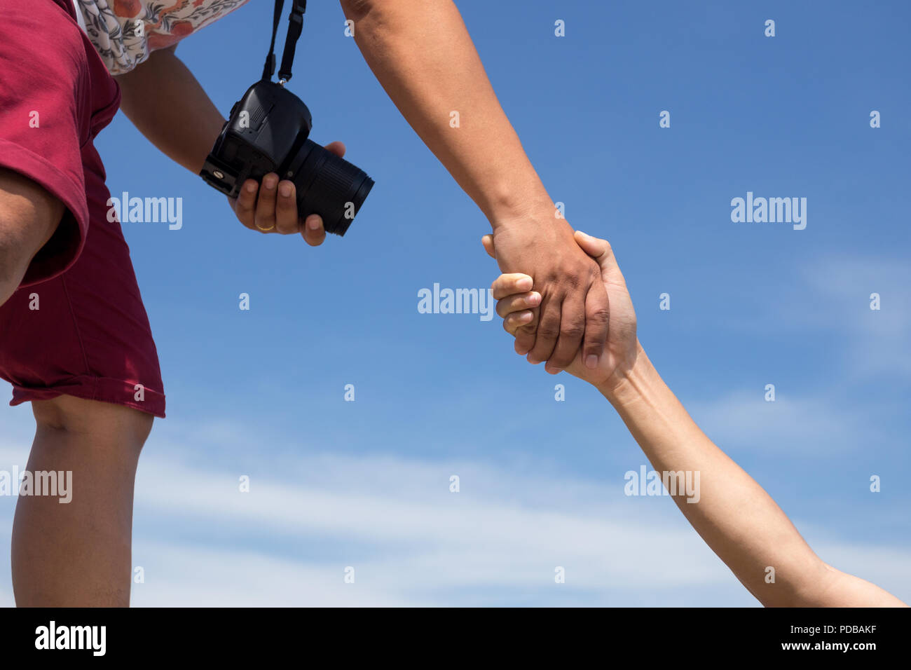 Man with camera helping friend climbing rock at the beach in blue sky ...