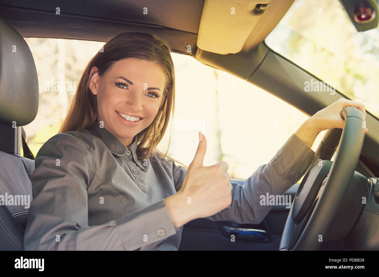 Happy young woman sitting inside of car and showing thumb up happy with ...