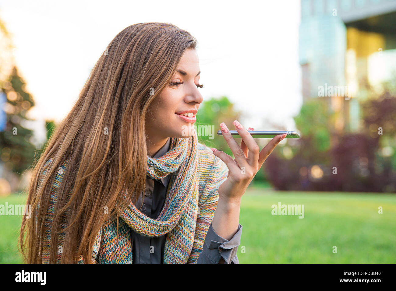 Charming young woman holding smartphone and giving voice command using ...