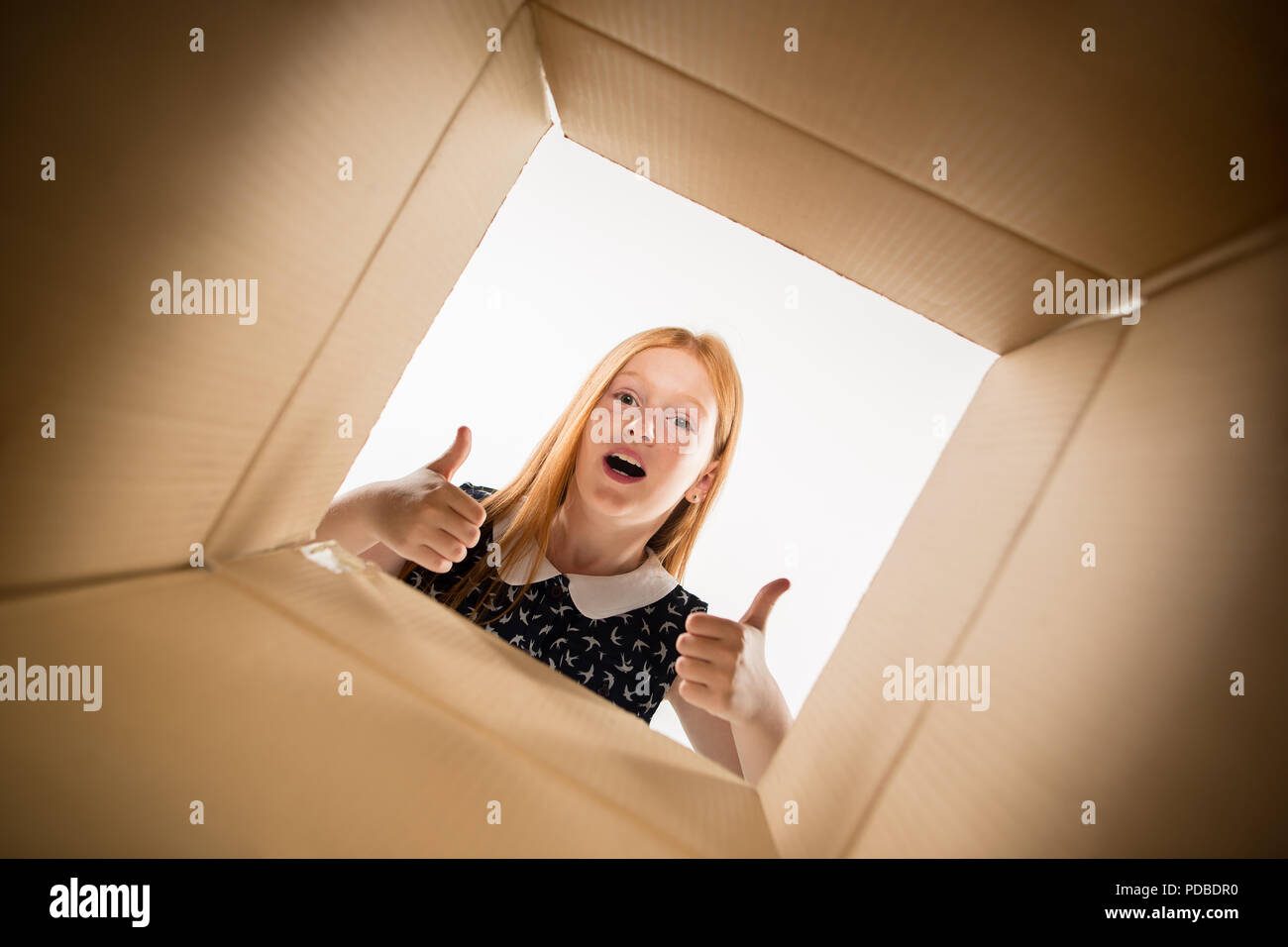 The surprised girl unpacking, opening carton box and looking inside ...