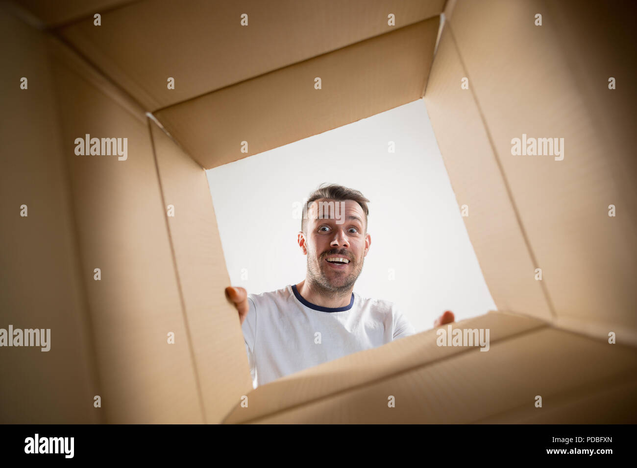 The surprised man unpacking, opening carton box and looking inside. The ...