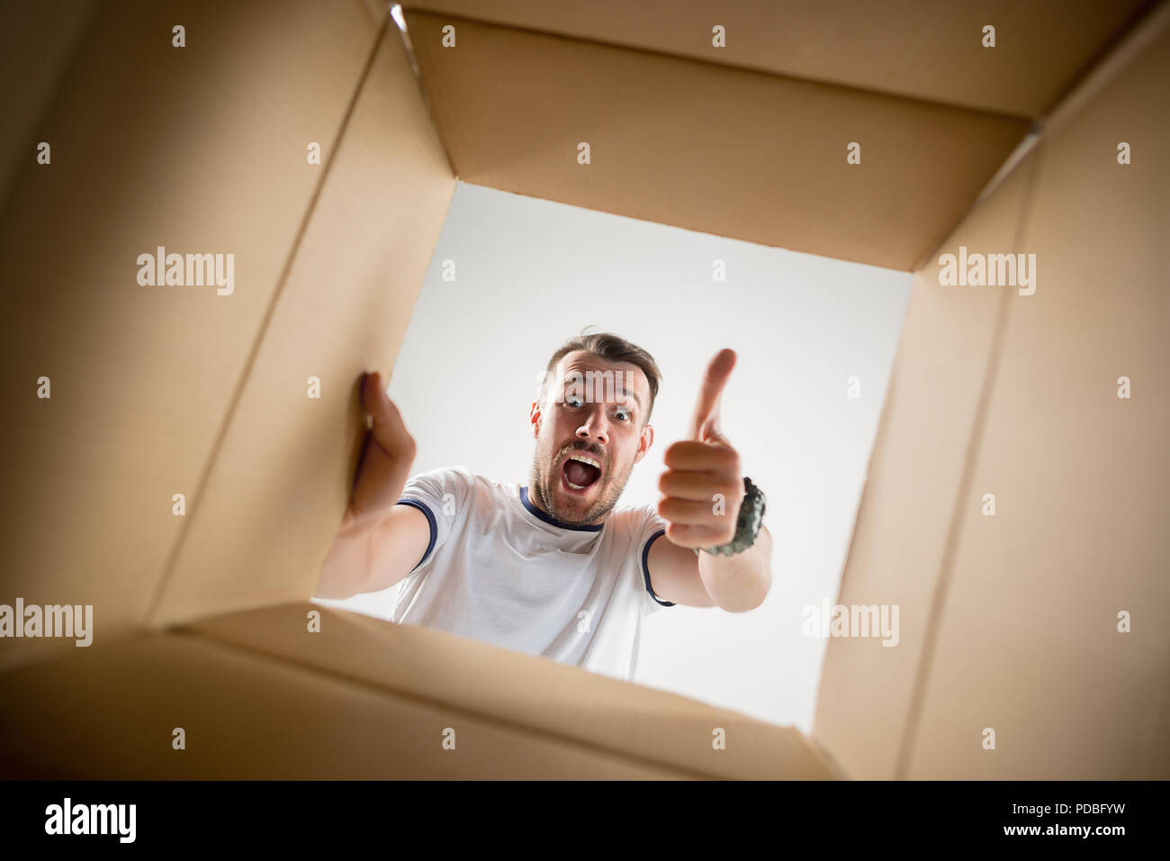 The surprised man unpacking, opening carton box and looking inside. The ...