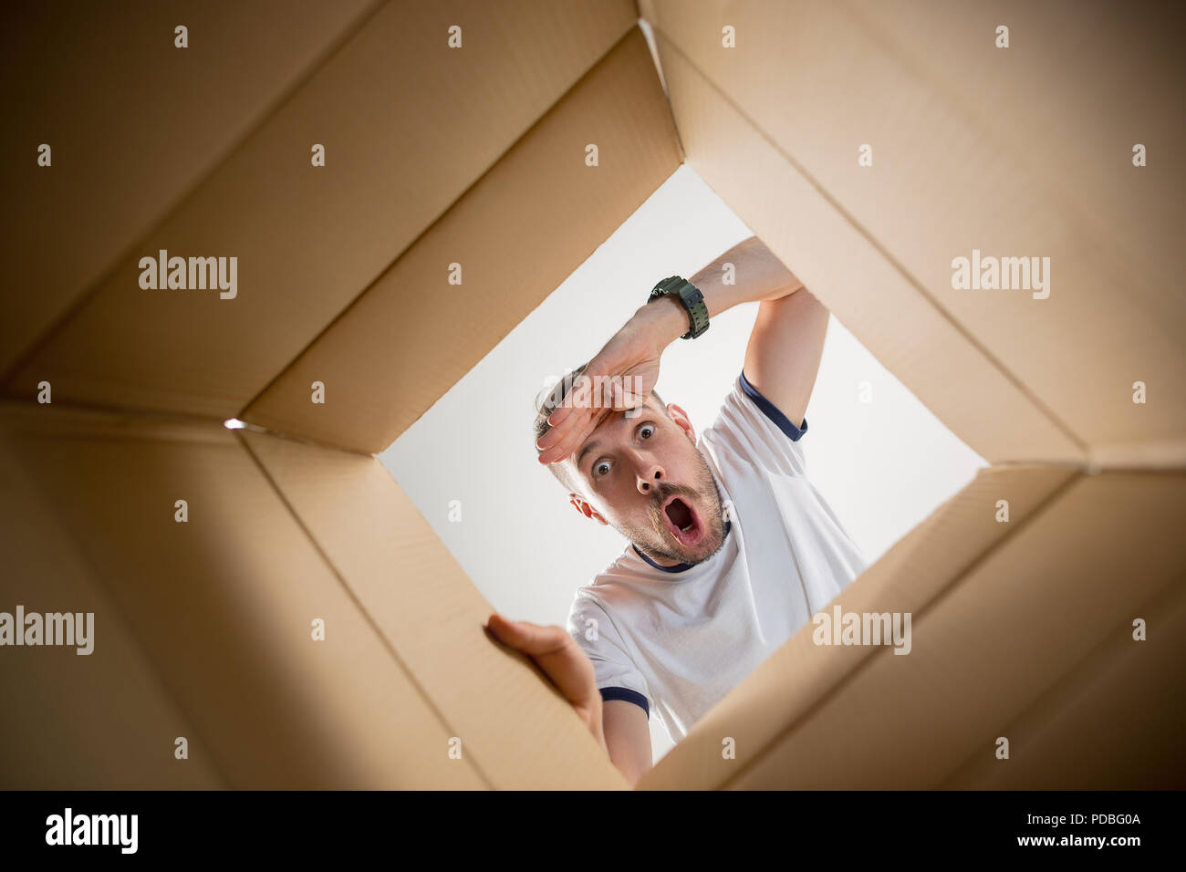 The surprised man unpacking, opening carton box and looking inside. The ...