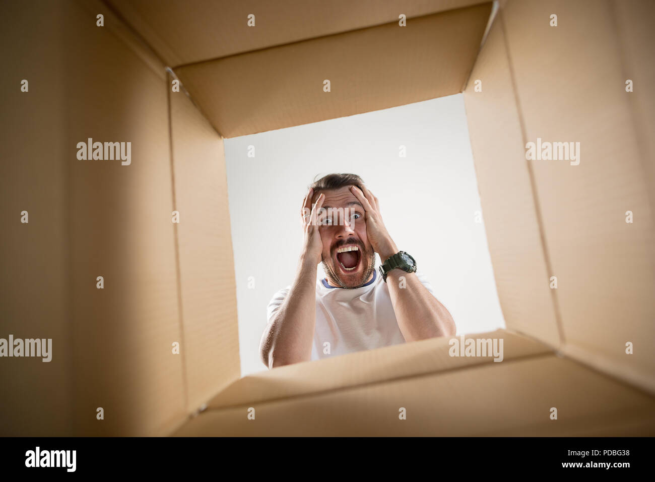 The surprised man unpacking, opening carton box and looking inside. The ...